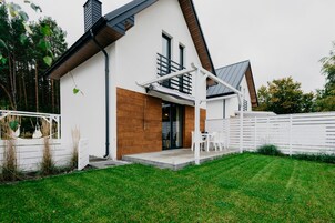 Uma casa moderna de dois andares com varanda coberta, deck de madeira e quintal cercado.