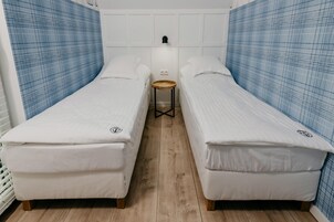 Quarto com duas camas de solteiro, uma mesa de madeira pequena e luminária fixada na parede.
