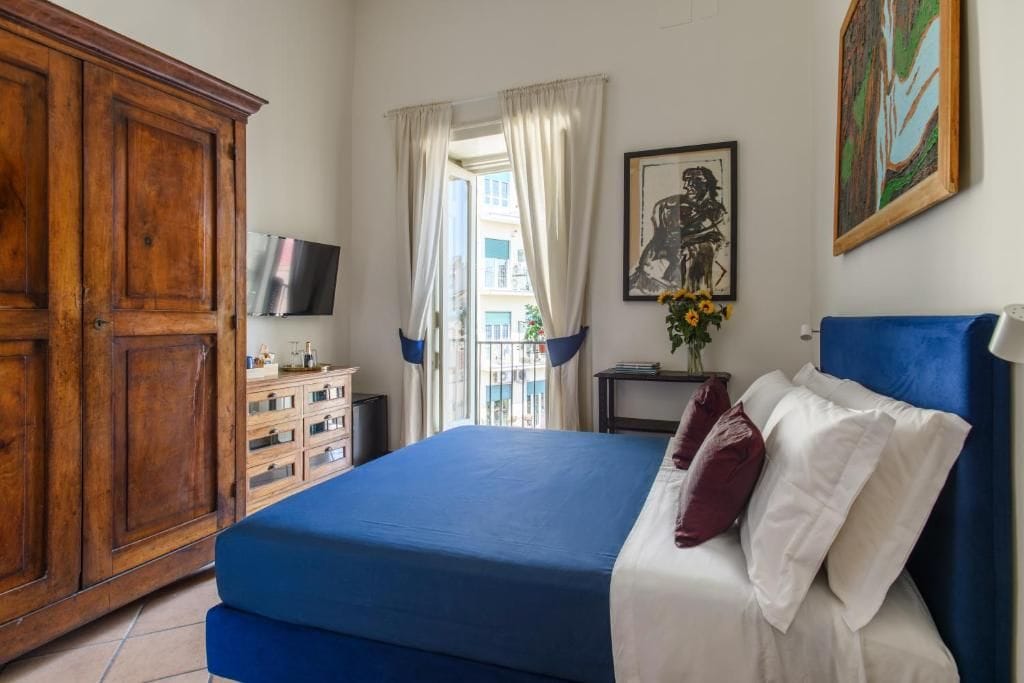 Quarto com cama, guarda-roupa de madeira, televisão e janela com cortinas.