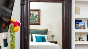 Quarto com espelho grande, cama com roupa de cama azul, mesa de cabeceira e um vaso com flores.