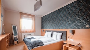 Quarto de hotel moderno com cama de madeira, mesa de cabeceira, espelho e janela com cortinas.