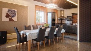 Uma sala de jantar com mesa posta para seis, cozinha ao fundo e um quadro na parede.