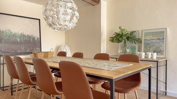 Uma área de jantar com uma mesa de madeira, cadeiras marrons, luminária pendente e quadros nas paredes.