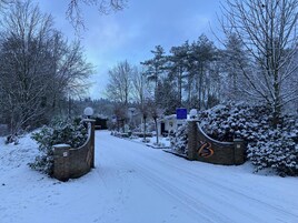 Um portão de entrada coberto de neve, com uma placa, um muro de tijolos e um edifício ao fundo.