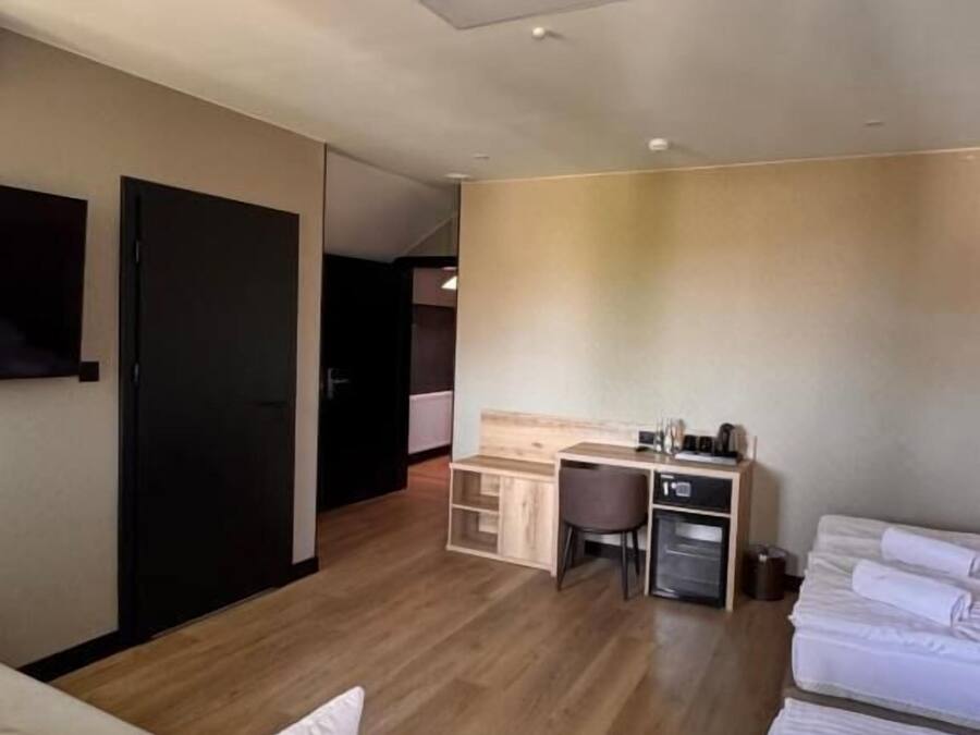 Quarto de hotel moderno com piso de madeira, sofá, cama, escrivaninha e cozinha compacta.