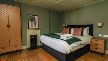 Quarto com cama, mesas de cabeceira, guarda-roupa, lareira e um quadro na parede.