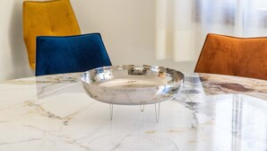 Mesa redonda de mármore com uma tigela metálica no centro, rodeada por cadeiras com assentos acolchoados.