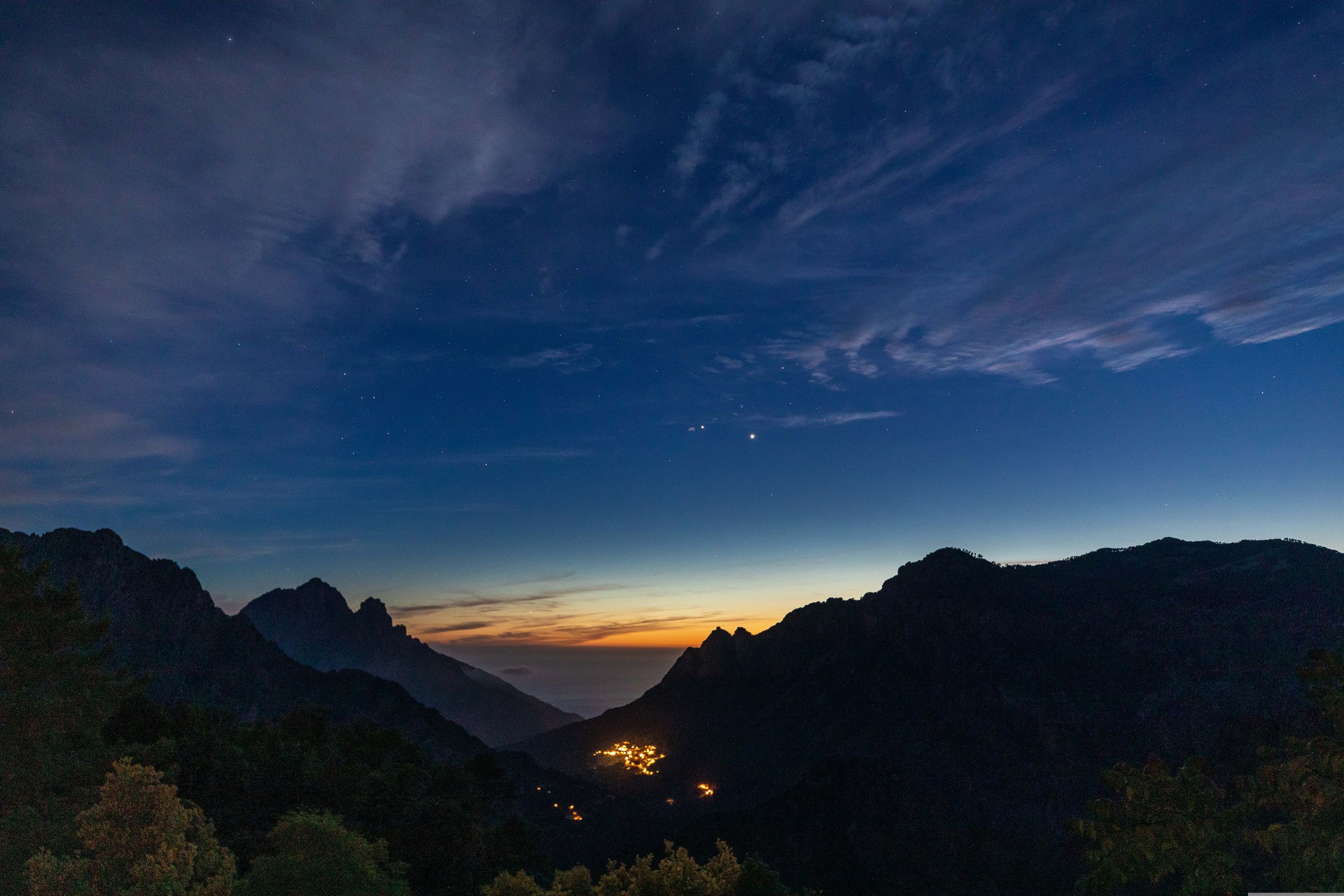 Paisagem montanhosa ao crepúsculo, com uma povoação visível no vale.