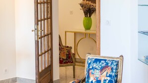 Uma porta aberta dá acesso a um quarto com uma cadeira, um vaso e um espelho.