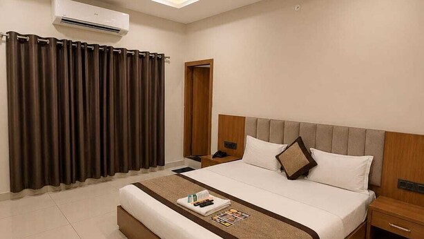 Quarto de hotel moderno com uma cama grande, mesa de cabeceira, ar condicionado e ventoinha no teto.