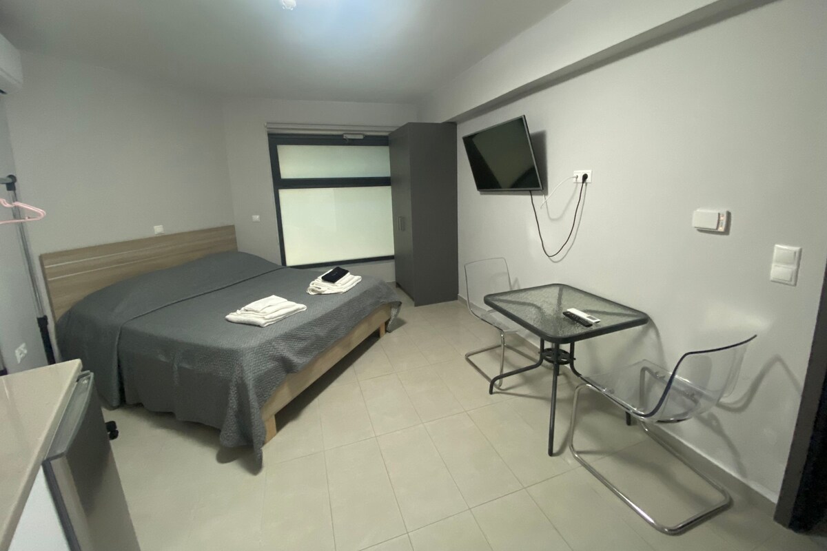 Quarto de hotel moderno com cama, televisão presa à parede, mesa pequena e cadeira.