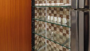 Cozinha com estante de vidro exibindo copos, geladeira de aço inoxidável e painel de azulejos estampado.