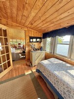 Uma cabana com interior de madeira, uma cama, uma escrivaninha e vista para um lago.