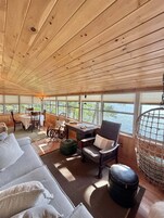Interior em madeira com um sofá, cadeiras, uma mesa e vista para o exterior.