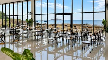 Uma ampla área de refeições interna com grandes janelas com vista para uma praia.