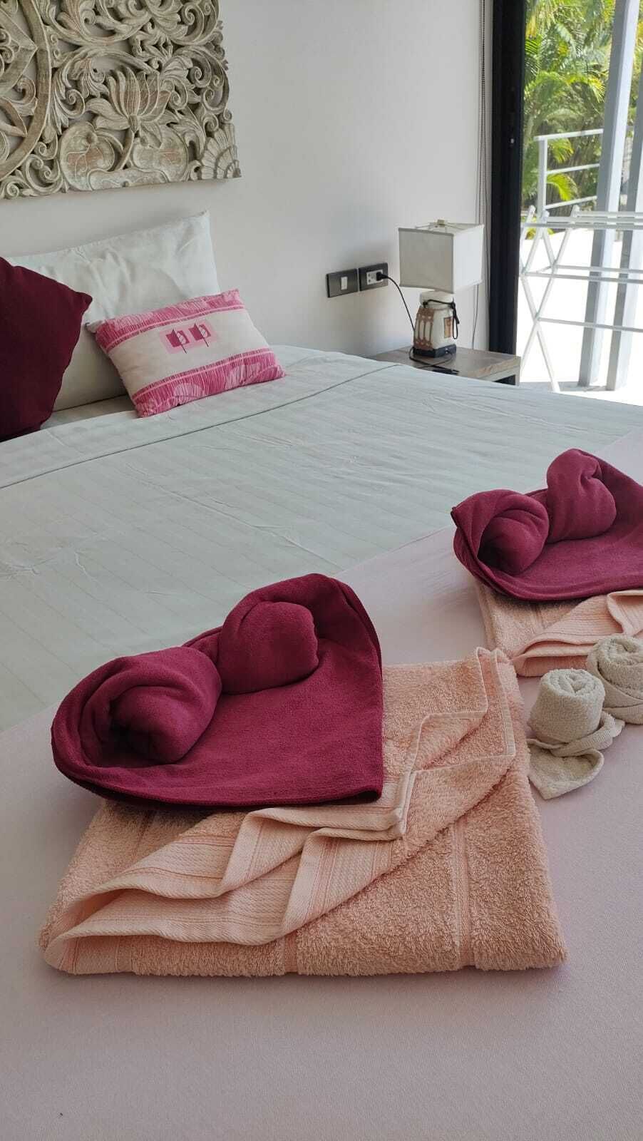 Cama bem arrumada com almofada decorativa, mesa de cabeceira com abajur e vista para o verde lá fora.