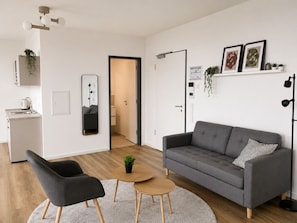 Uma sala de estar moderna com um sofá cinzento, uma poltrona preta, uma mesa de centro pequena e um tapete redondo.