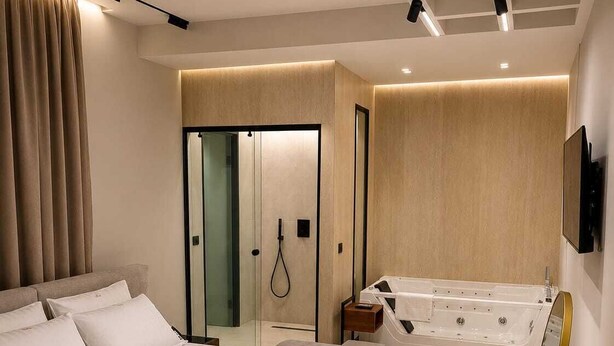 Quarto moderno com cama grande, chuveiro amplo, banheira e mesa de cabeceira de madeira.
