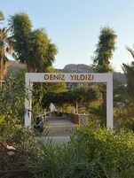 Um sinal com a inscrição 'DENİZ YILDIZ', rodeado por vegetação e uma paisagem montanhosa ao fundo.
