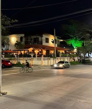 Um edifício com um grande letreiro iluminado, área de estar coberta ao ar livre e uma rua com veículos.