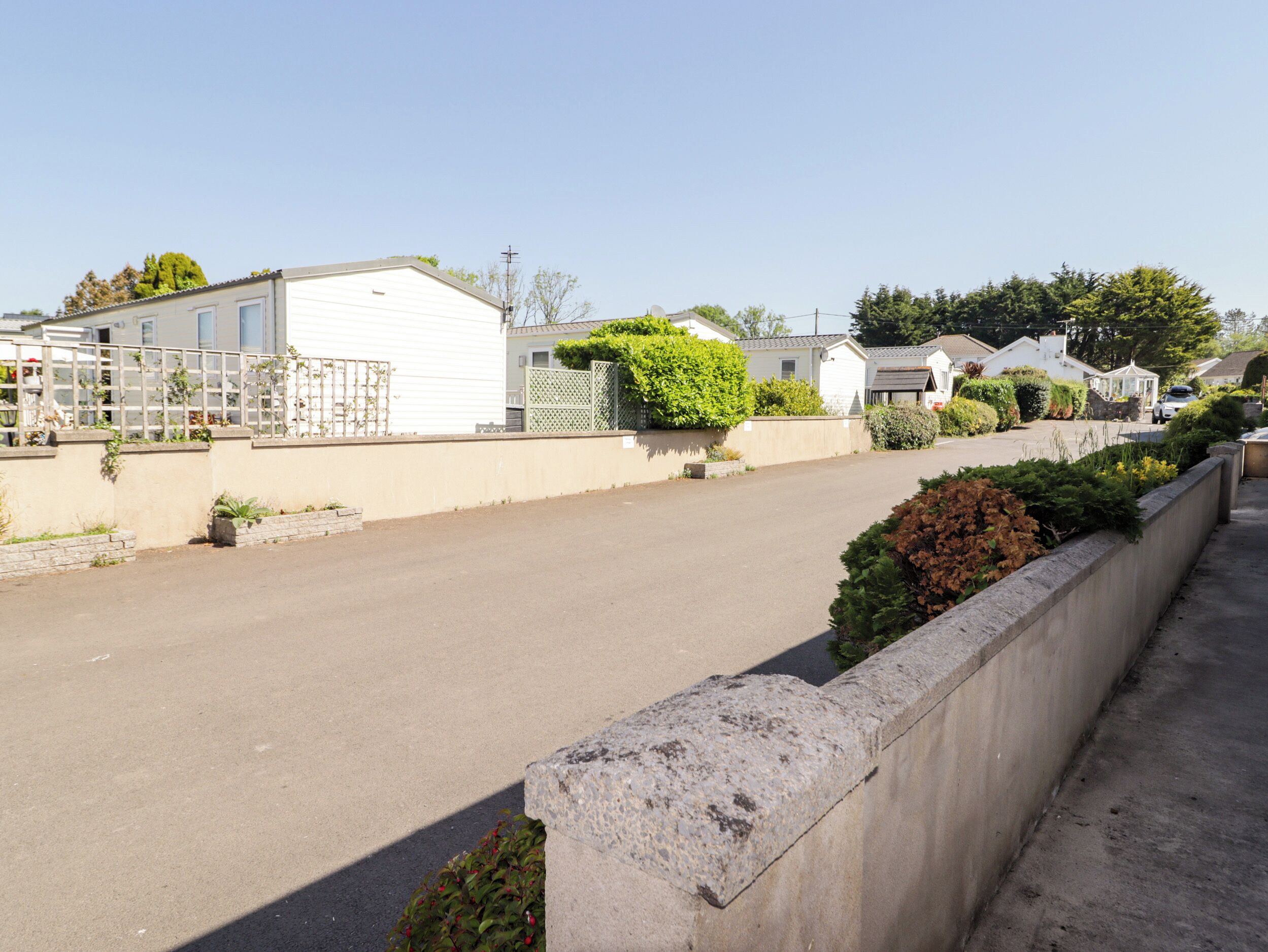 Rua residencial com casas, céu claro e calçada de concreto.