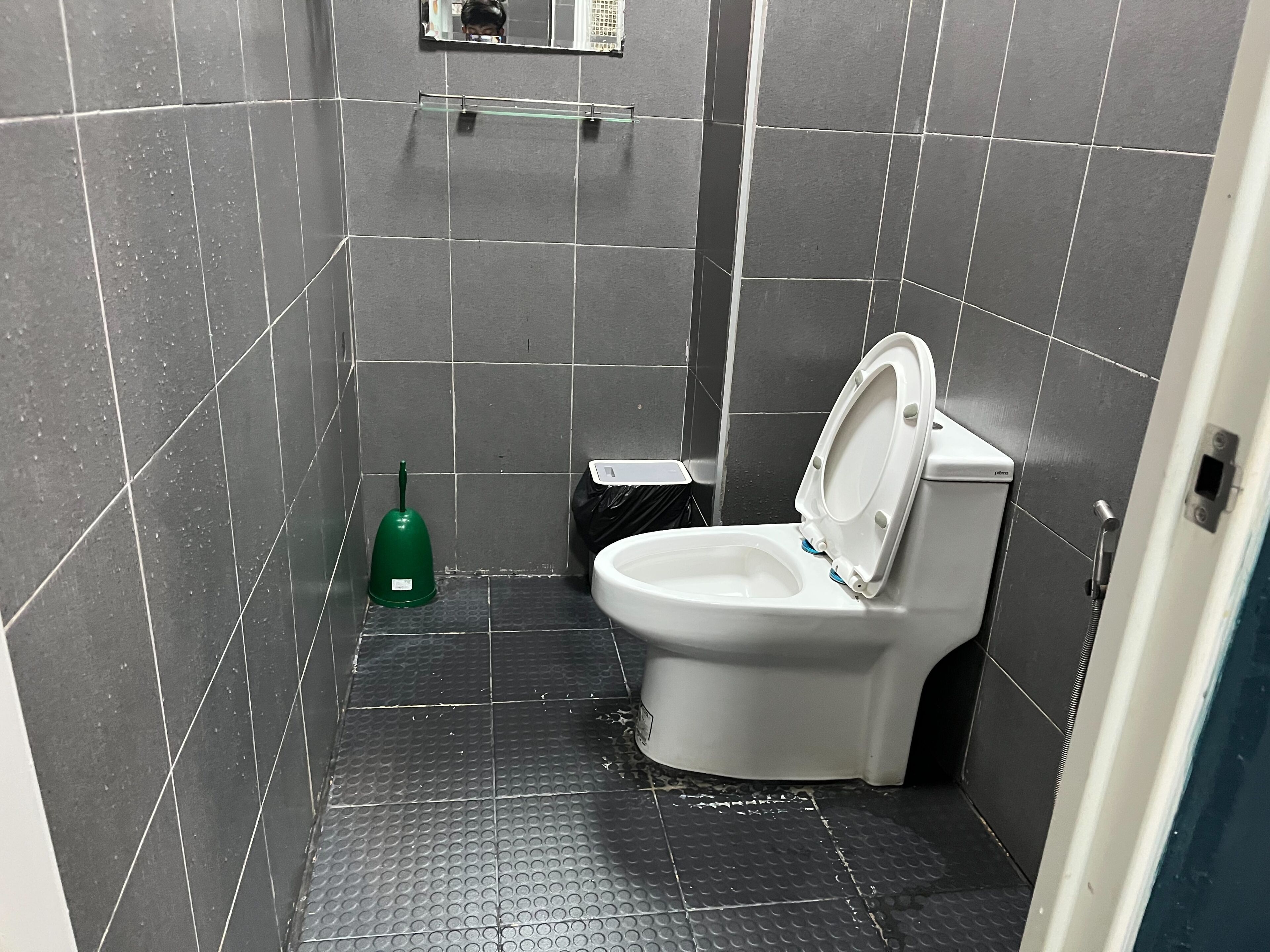 Um banheiro pequeno com vaso sanitário, um desentupidor verde e uma lixeira.