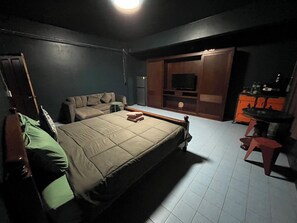 Quarto com cama, sofá, televisão e uma pequena mesa.