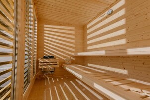 Uma sauna com ripas de madeira nas paredes e no teto, um banco e uma pequena mesa com um balde.