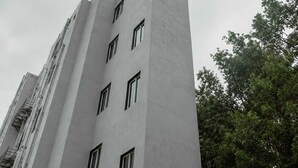 Um edifício moderno com um letreiro dourado destacado no topo, várias janelas e uma entrada visível com interior iluminado.