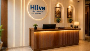 Balcão de recepção de hotel com uma placa indicando 'Hiive By Convivial HOTEL', um laptop, uma placa de recepção e duas fotos emolduradas na parede.
