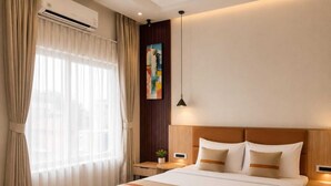 Quarto de hotel com cama, cortinas, quadro, mesa de cabeceira e abajur.