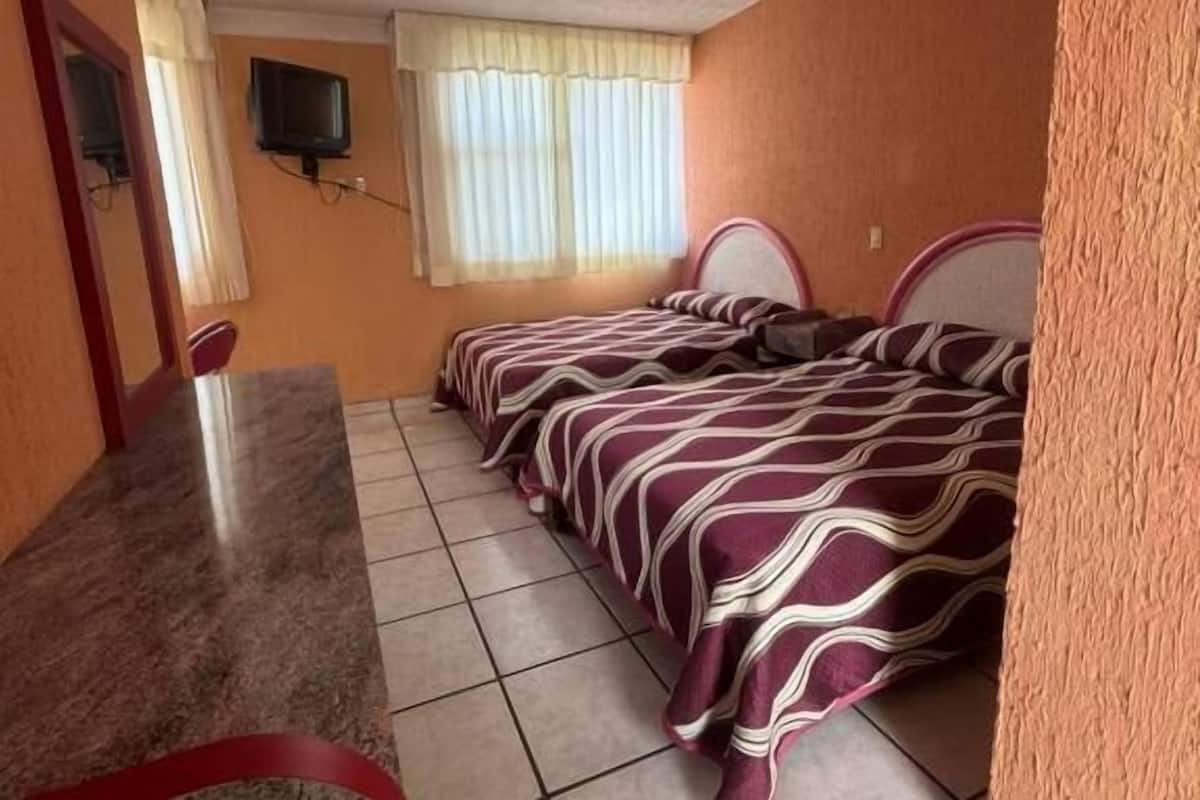 Quarto com uma cama, ventilador de teto, televisão e janela com cortinas.