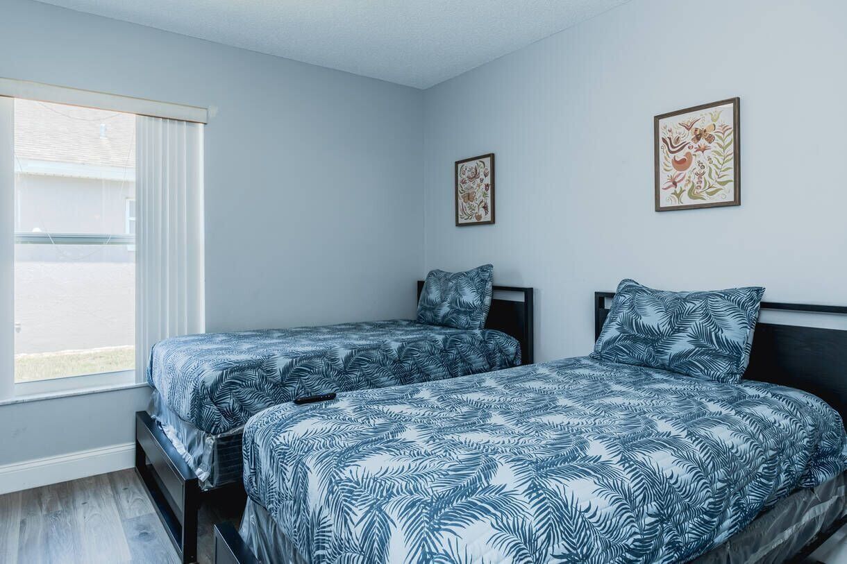 Quarto com duas camas, uma janela e duas obras de arte emolduradas na parede.