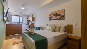 Quarto de hotel com cama, mesa de cabeceira, escrivaninha com cadeira, janela e vista da cidade.