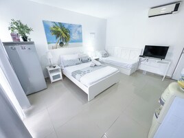 Quarto com cama, televisão, frigorífico e ar condicionado fixado na parede.