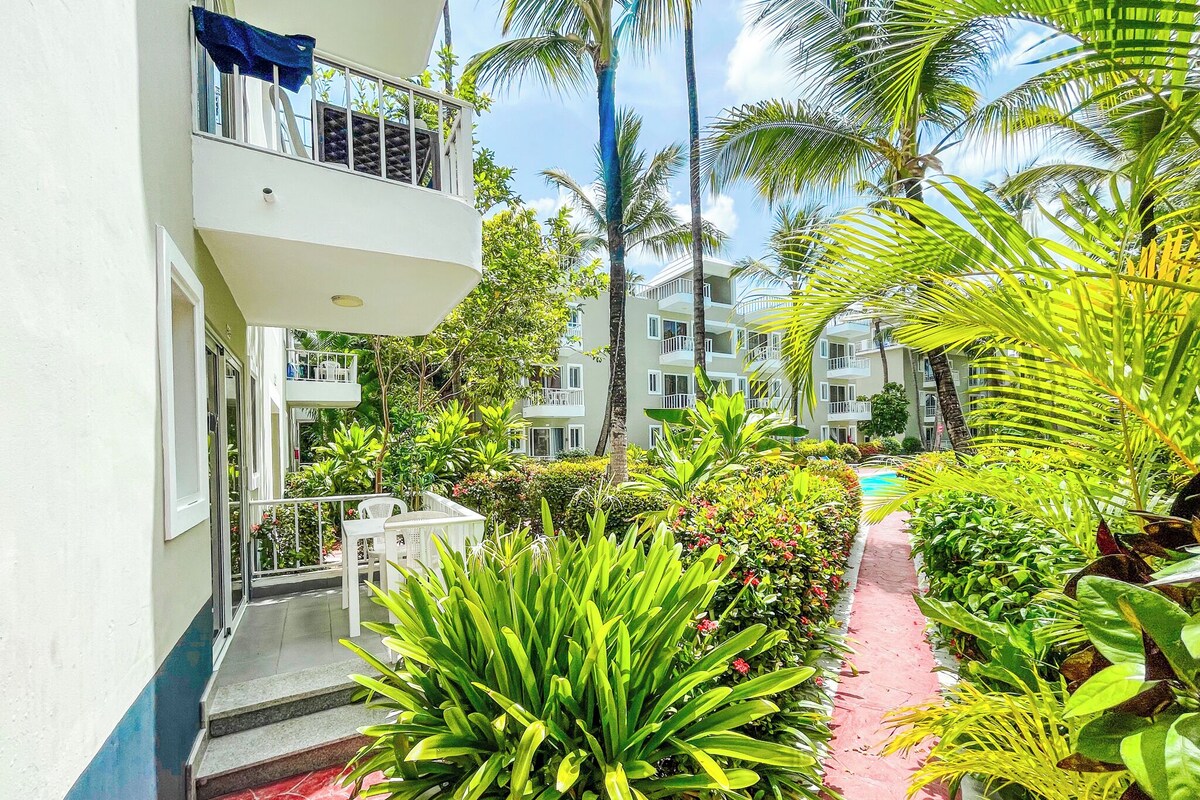 Pátio de hotel com piscina, cercado por vegetação exuberante e palmeiras.