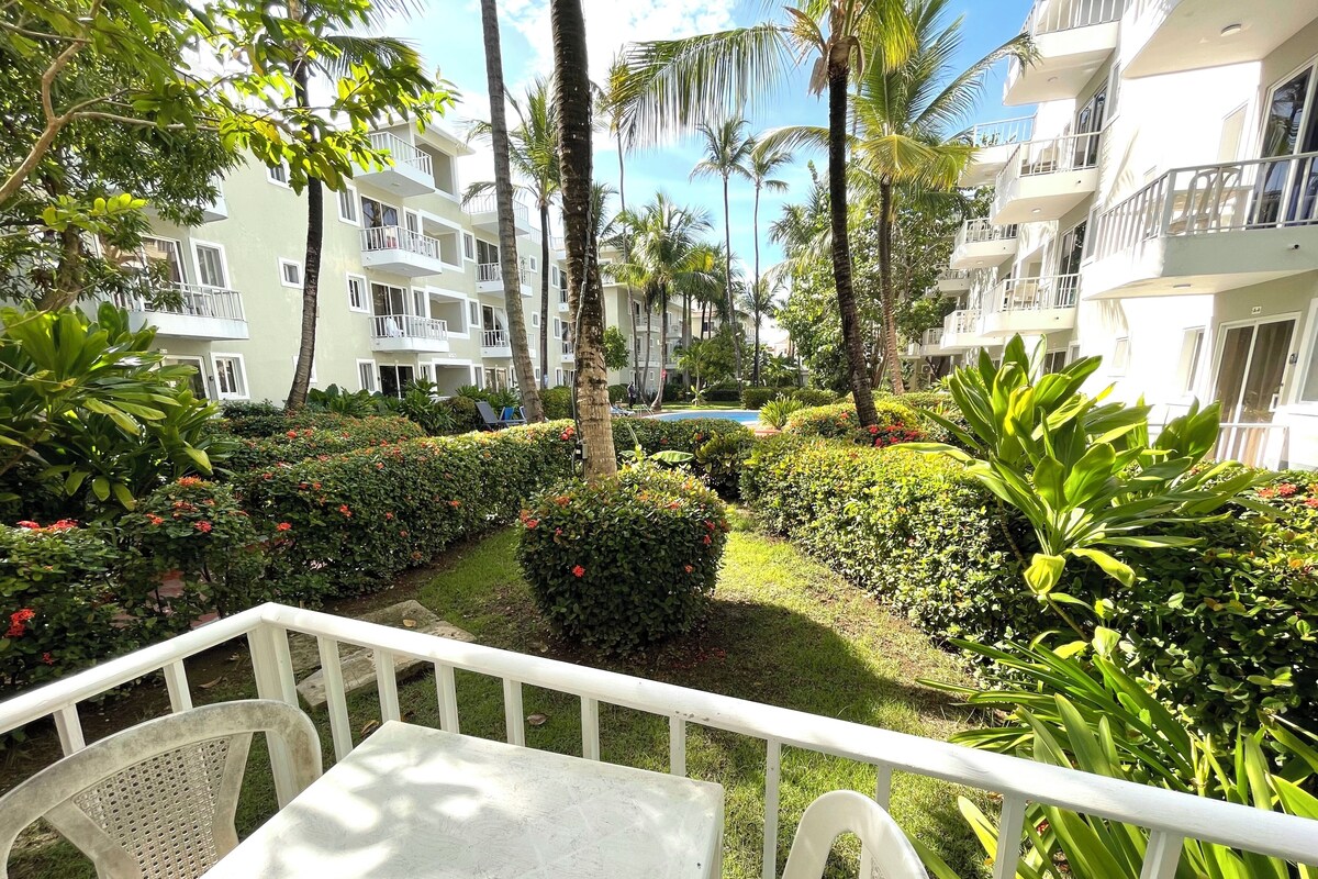 Pátio de hotel com piscina, palmeiras e guarda-corpo branco.