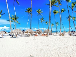 Praia com palmeiras e guarda-sóis de palha.