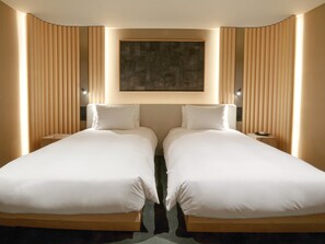 Quarto de hotel com duas camas de solteiro, uma grande obra de arte sobre as camas e design moderno com persianas verticais.