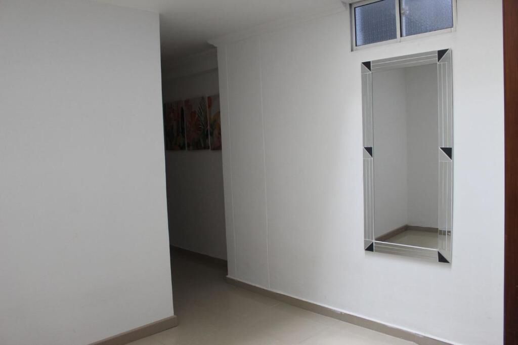 Um corredor com paredes brancas, uma porta no final e uma janela com vista.
