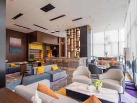 Um lobby moderno de hotel com área de bar, assentos e uma grande janela que oferece luz natural.