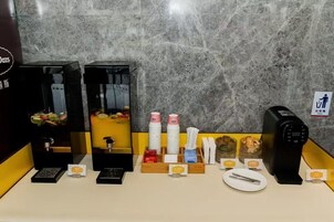 Uma estação de bebidas com serviço próprio, incluindo uma máquina de café, um dispensador de bebidas e uma lixeira.