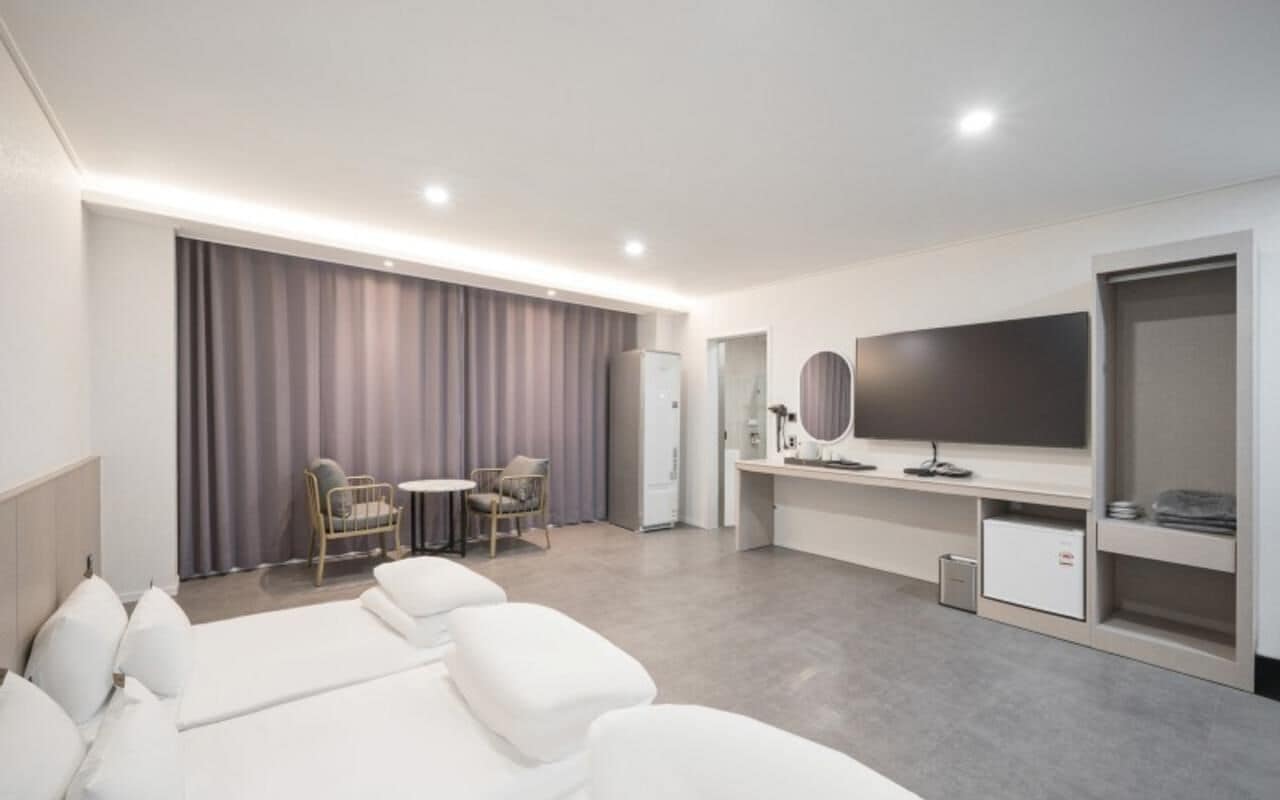 Quarto de hotel moderno com cama, televisão, escrivaninha e área de estar.