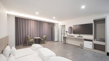 Quarto de hotel moderno com cama, televisão, escrivaninha e área de estar.