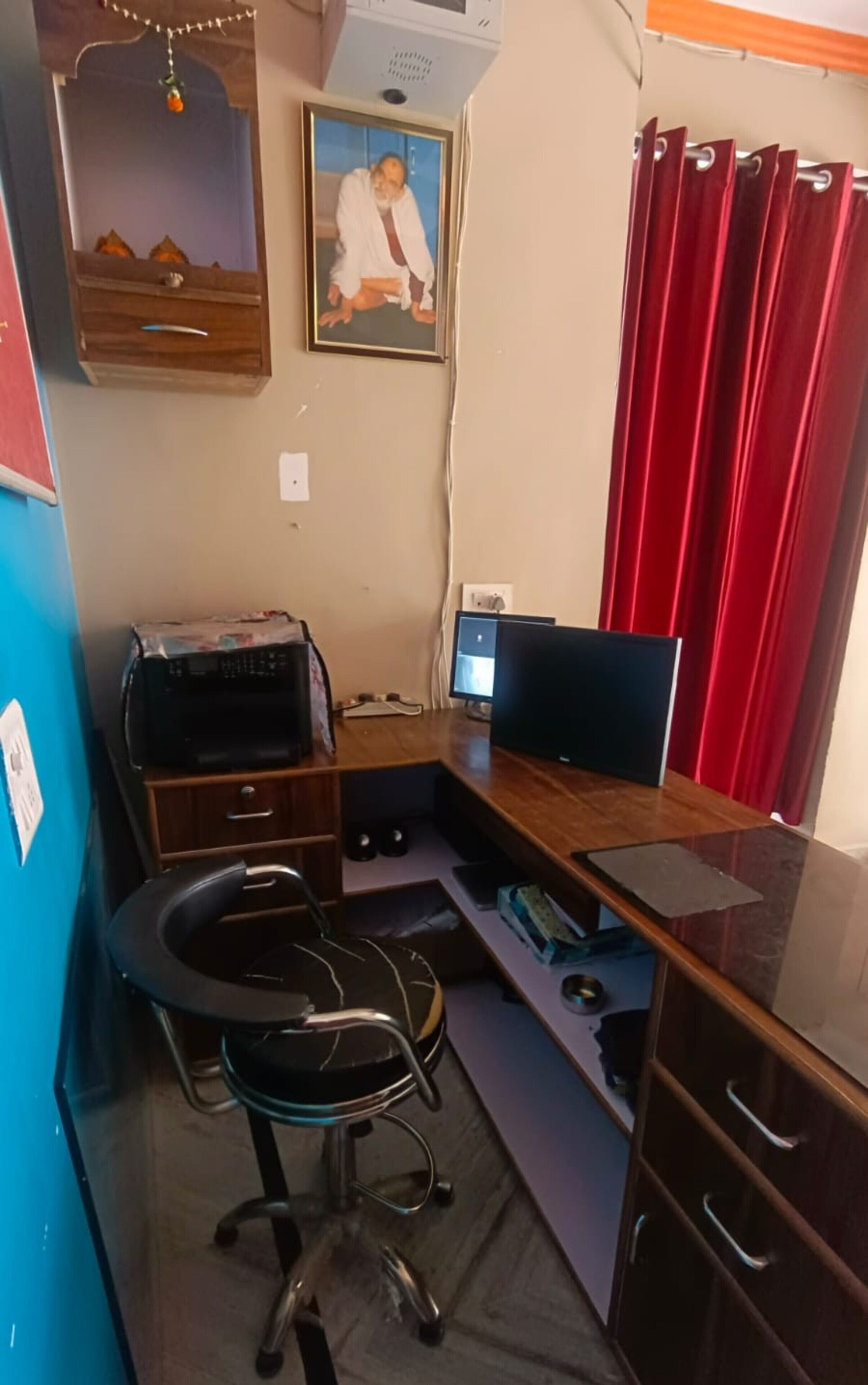 Um espaço de escritório pequeno, com escrivaninha, cadeira, computador e uma prateleira.