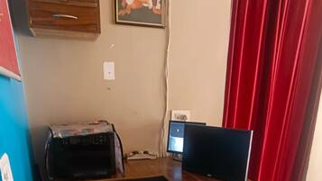 Um espaço de escritório pequeno, com escrivaninha, cadeira, computador e uma prateleira.