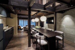 Cozinha moderna com armários de madeira escura, ilha central com assentos, iluminação pendente e vista para um espaço japonês tradicional.