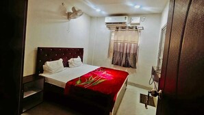 Quarto com cama, ventoinha no teto, ar condicionado, janela com cortinas e porta com puxador.