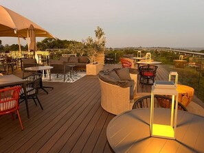 Um terraço no telhado com área de estar ao ar livre, incluindo mesas e cadeiras, e vista para a cidade.