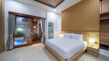 Quarto de hotel moderno com uma cama grande, mesa de cabeceira com abajur, porta de vidro deslizante para uma varanda e cabeceira de madeira.
